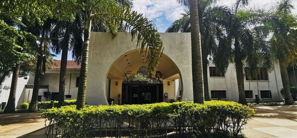 Um edifício com um arco central, rodeado por palmeiras e arbustos bem cuidados.