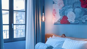 Quarto com cama, pintura de rosas, janela com cortinas e luminária pendente.