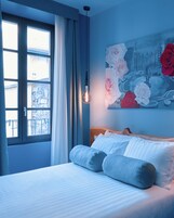 Quarto com cama, pintura de rosas, janela com cortinas e luminária pendente.