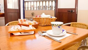 Uma mesa de jantar de madeira com uma cesta de pão, uma xícara com um desenho floral e uma pequena tigela de doces.