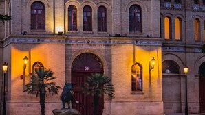 Um edifício histórico com uma entrada arqueada imponente, número 59, e uma estátua de um homem e um animal em frente.