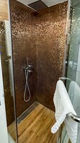 Uma casa de banho moderna com cabine de chuveiro em vidro, uma toalha branca e parede revestida a azulejos.
