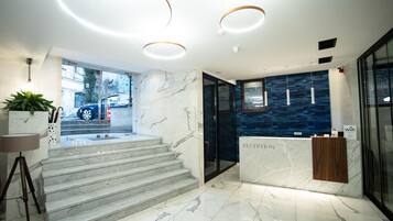 Uma área de recepção moderna com degraus de mármore que levam ao balcão, uma grande janela com vista para a rua e uma parede azul com textura.