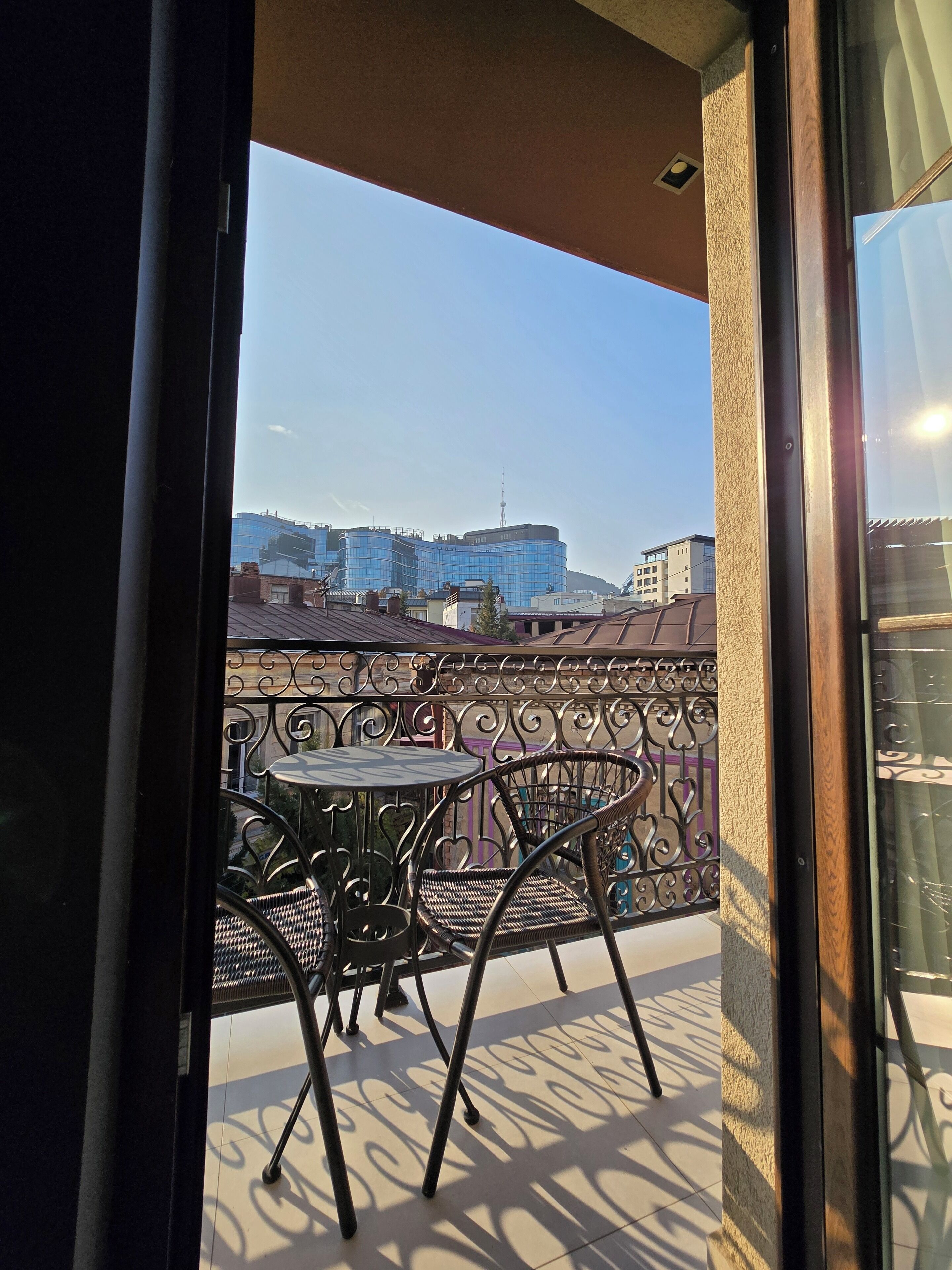 Uma varanda com vista para a paisagem urbana, com guarda-corpo de metal e uma mesa com cadeiras.
