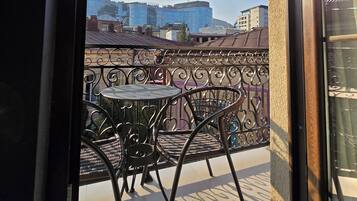Uma varanda com vista para a paisagem urbana, com guarda-corpo de metal e uma mesa com cadeiras.