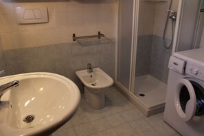 Casa de banho com lavatório, bidé, chuveiro e máquina de lavar roupa.