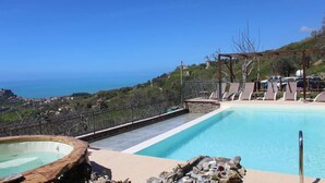 Área da piscina com vista para o mar, uma banheira de hidromassagem e espreguiçadeiras.
