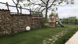 Um muro de pedra, um parquinho com escorrega e um caminho pavimentado.