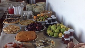 Uma mesa de buffet com diversos alimentos, incluindo tortas, doces, frutas e pão.