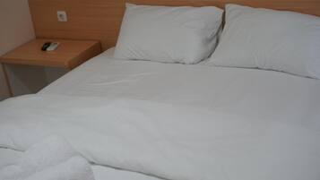 Uma cama com roupa de cama branca, cabeceira de madeira e mesa de cabeceira com controle remoto.