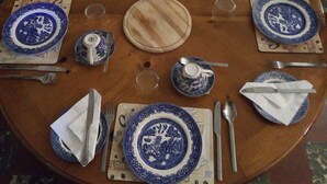 Mesa posta com pratos azul e branco, talheres e um jarro de suco de laranja.
