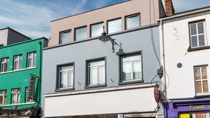 Um edifício com vários andares e uma mistura de estilos arquitetônicos, incluindo uma fachada verde e uma seção superior branca.