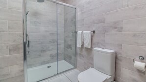 Um banheiro moderno com chuveiro em cabine de vidro, vaso sanitário e porta-toalhas.