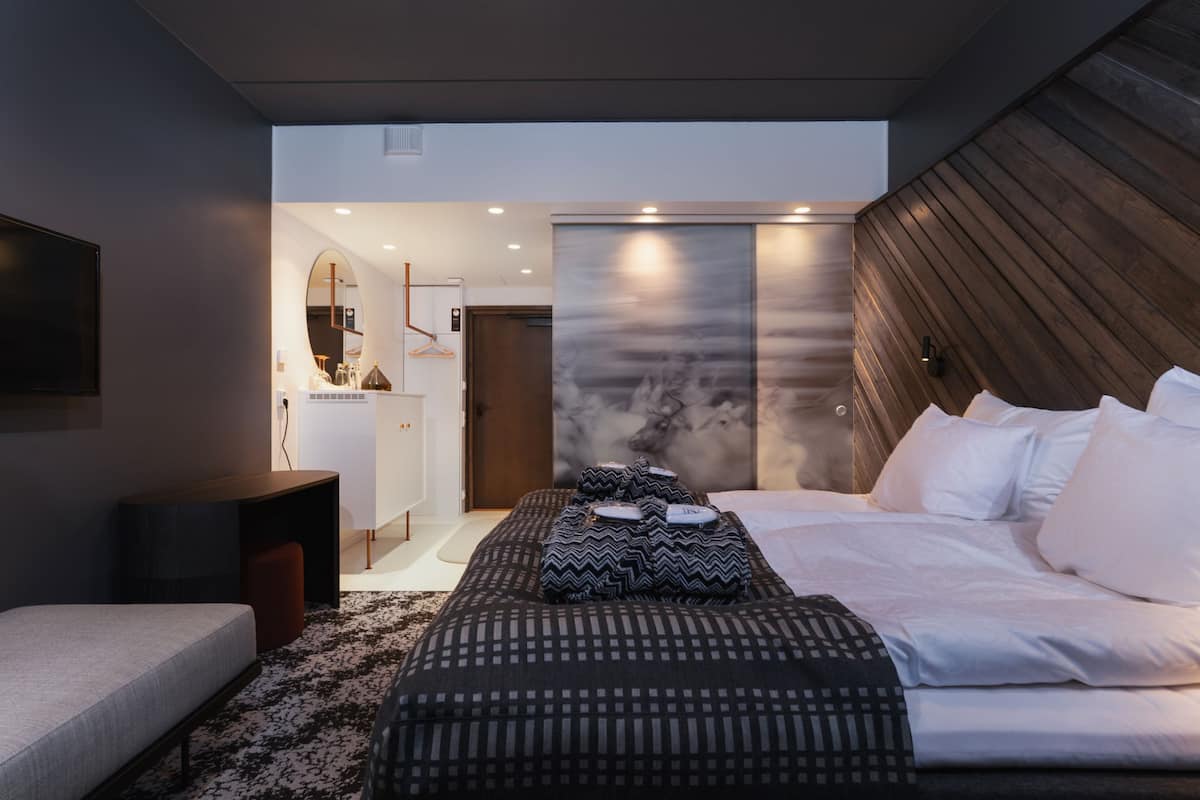 Quarto de hotel moderno com cama, área de estar, guarda-roupa e banheiro visível por uma porta aberta.