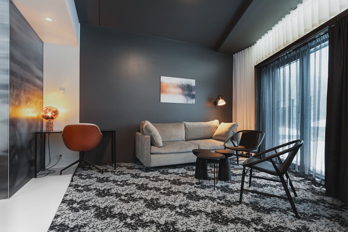 Uma sala de estar moderna com um sofá cinza, uma poltrona vermelha e uma mesa de centro preta. Há um quadro na parede e um abajur na mesinha lateral.