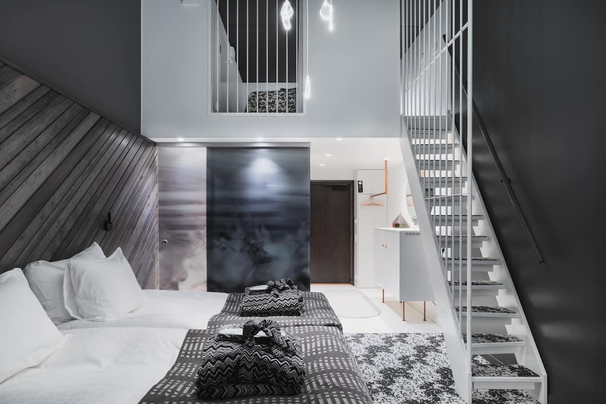 Quarto de hotel moderno com cama, escada e vista do céu.