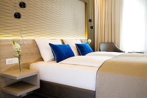 Quarto de hotel moderno com cama bem arrumada, mesa de cabeceira com um vaso de flores e uma cadeira.