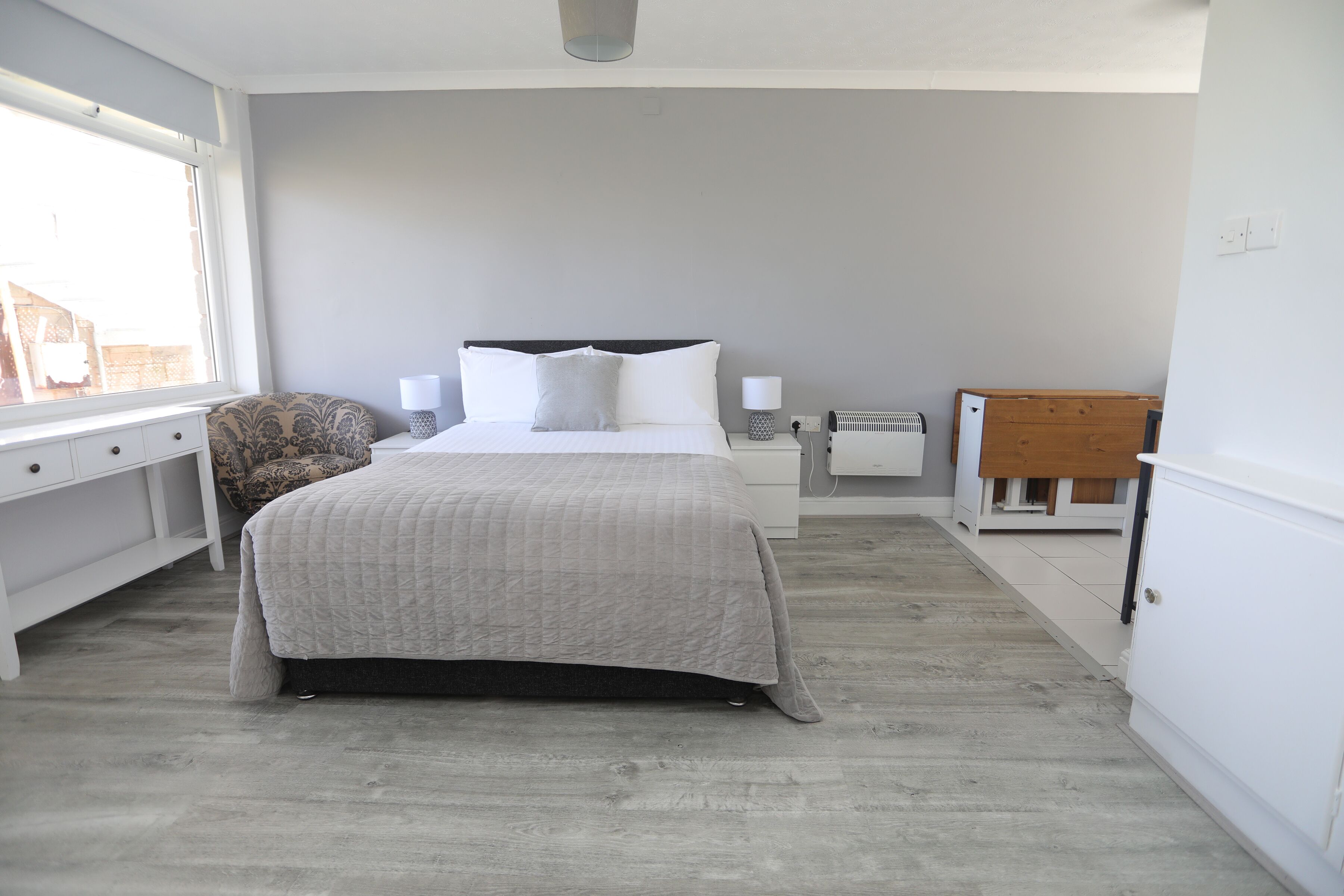 Quarto com cama, mesas de cabeceira, uma cadeira, aquecedor e janela.