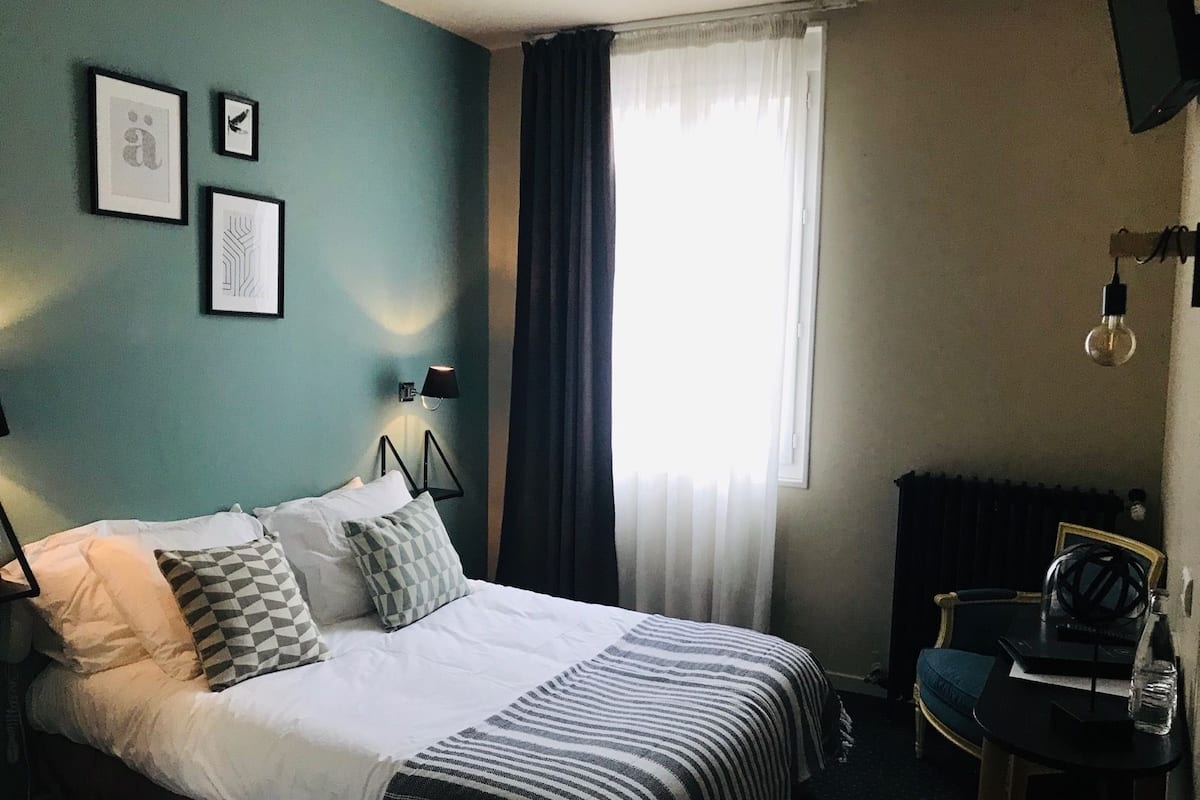 Uma cama bem arrumada com um cobertor listrado, uma escrivaninha com uma cadeira e uma janela com cortinas.