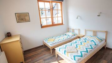 Quarto com duas camas de solteiro, penteadeira de madeira, janela e luminária na parede.