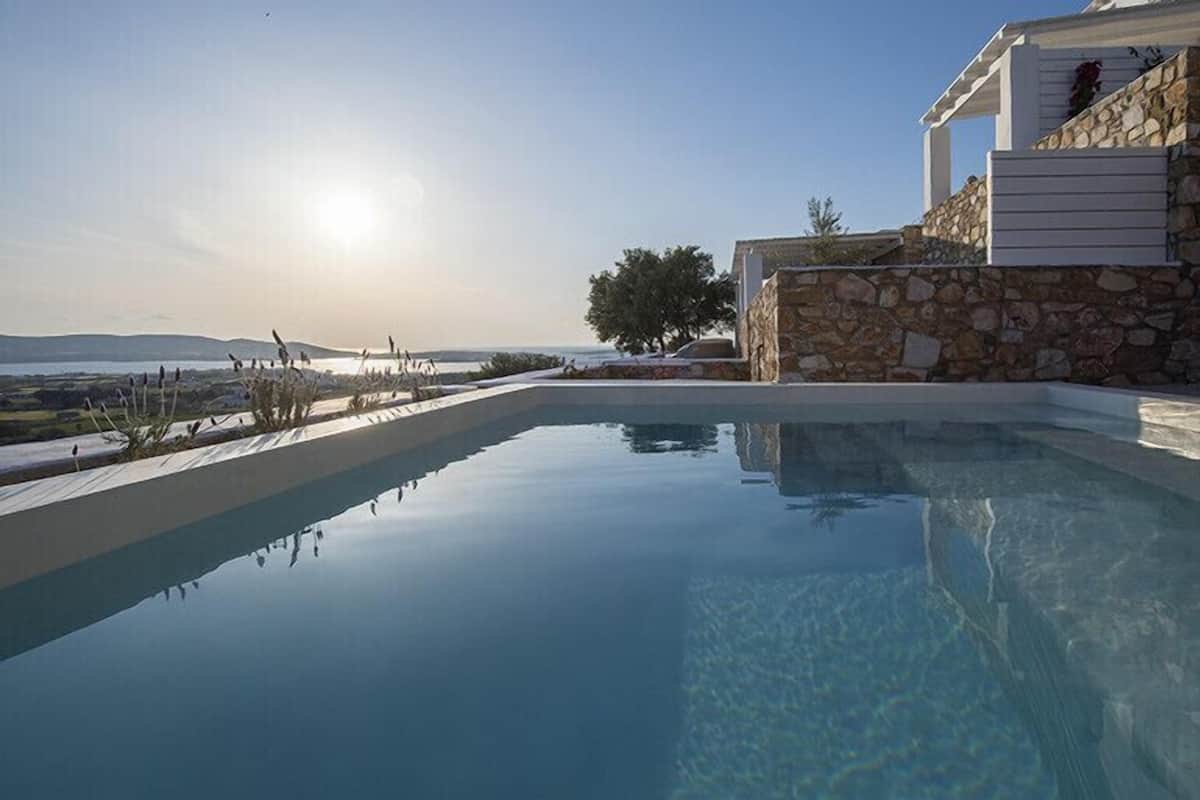 Piscina moderna com vista clara para o mar e um edifício de pedra com fachada branca.