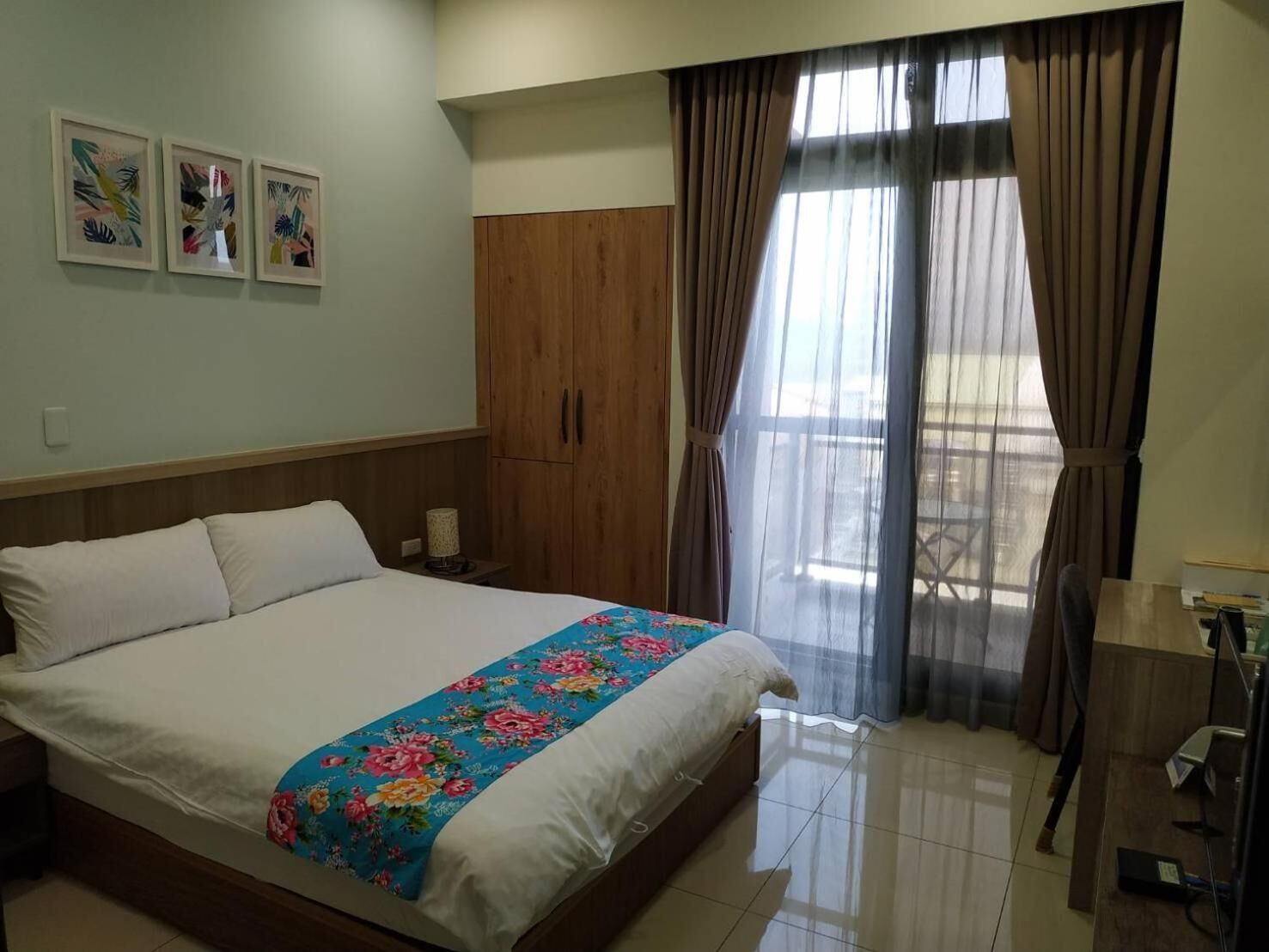 Quarto de hotel com cama, guarda-roupa de madeira, escrivaninha com cadeira e janela com cortinas.