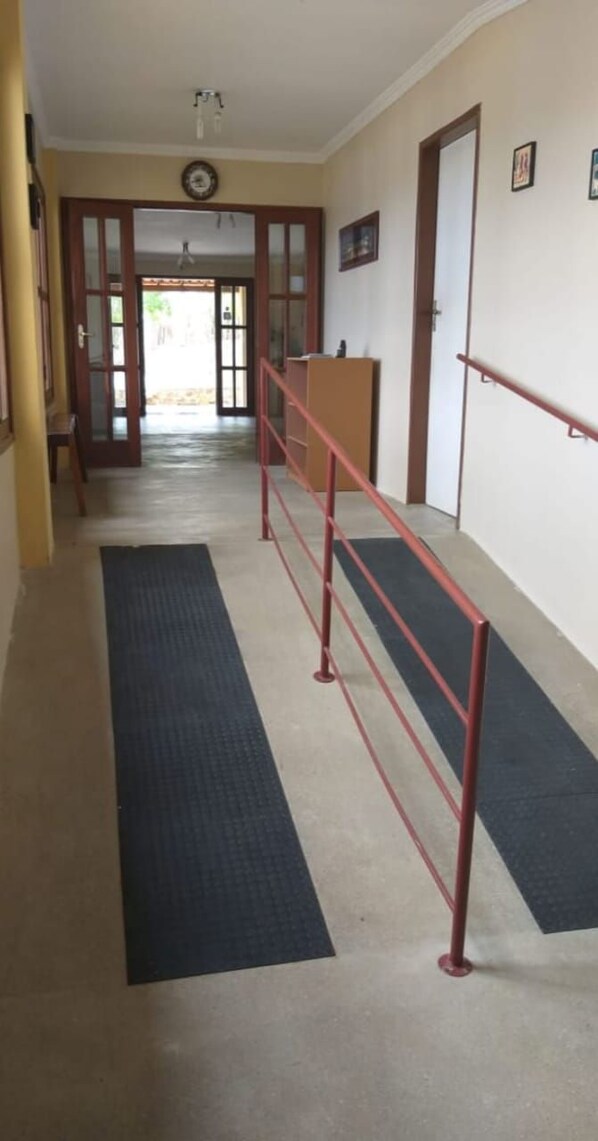 Corredor com corrimão vermelho, tapete no chão e uma porta no final.