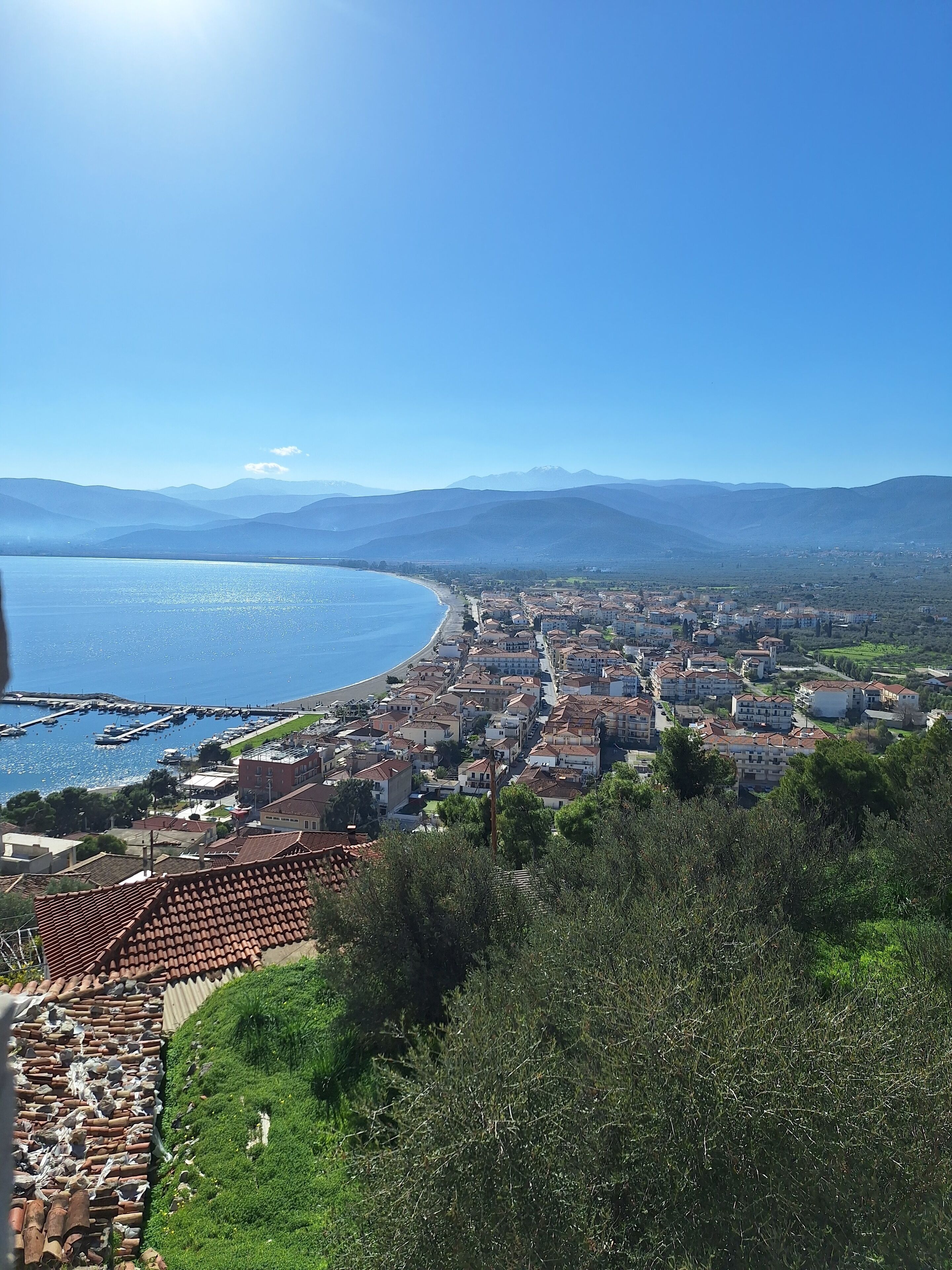 Uma vila costeira com um porto de recreio, casas em socalcos e montanhas ao fundo.