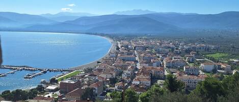 Uma vila costeira com um porto de recreio, casas em socalcos e montanhas ao fundo.