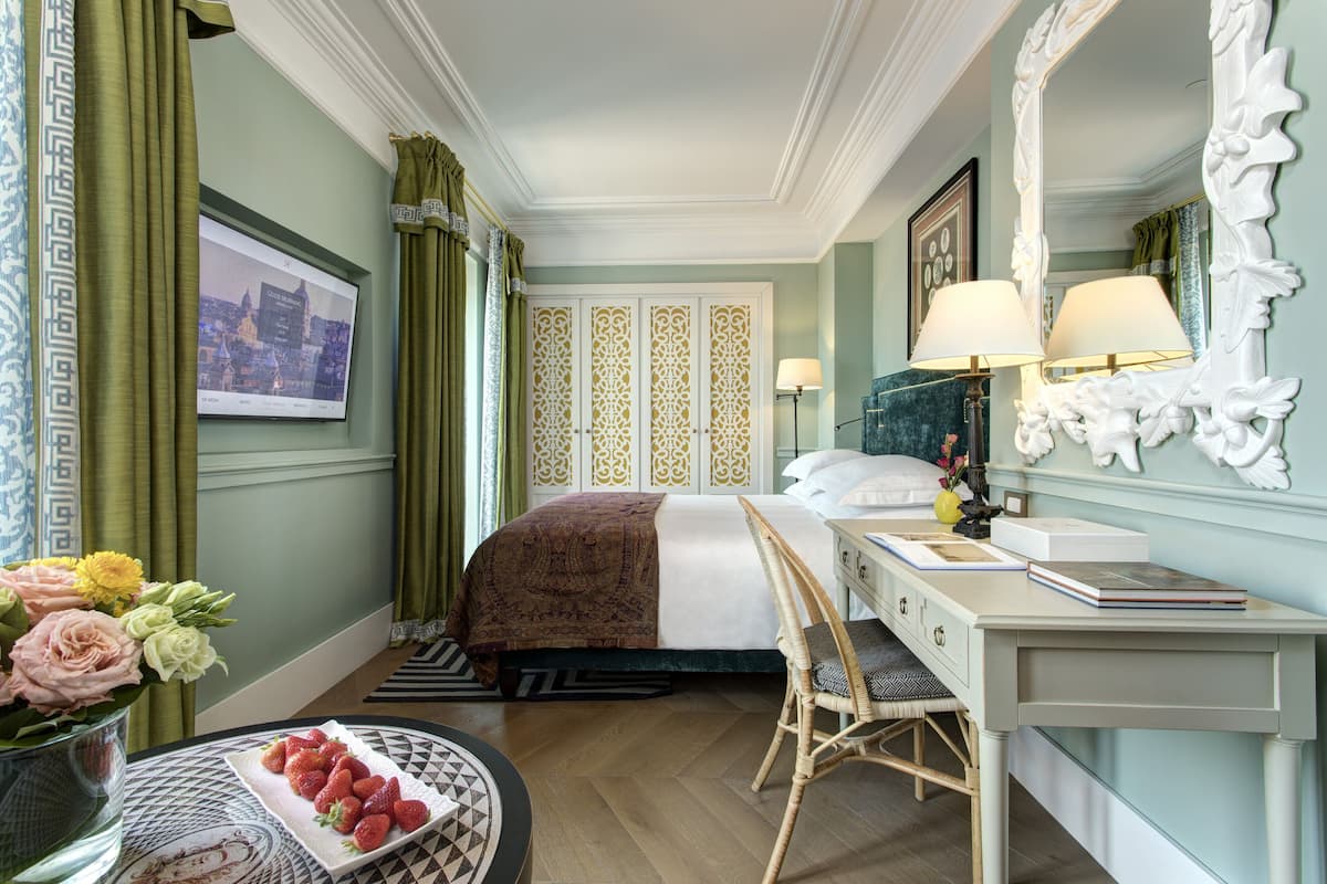 Quarto de hotel com cama, escrivaninha, cadeira e vista para a paisagem urbana pela janela.