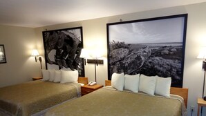 Quarto de hotel com duas camas, cada uma com cabeceira, mesas de cabeceira, luminárias e um grande quadro com paisagem na parede.