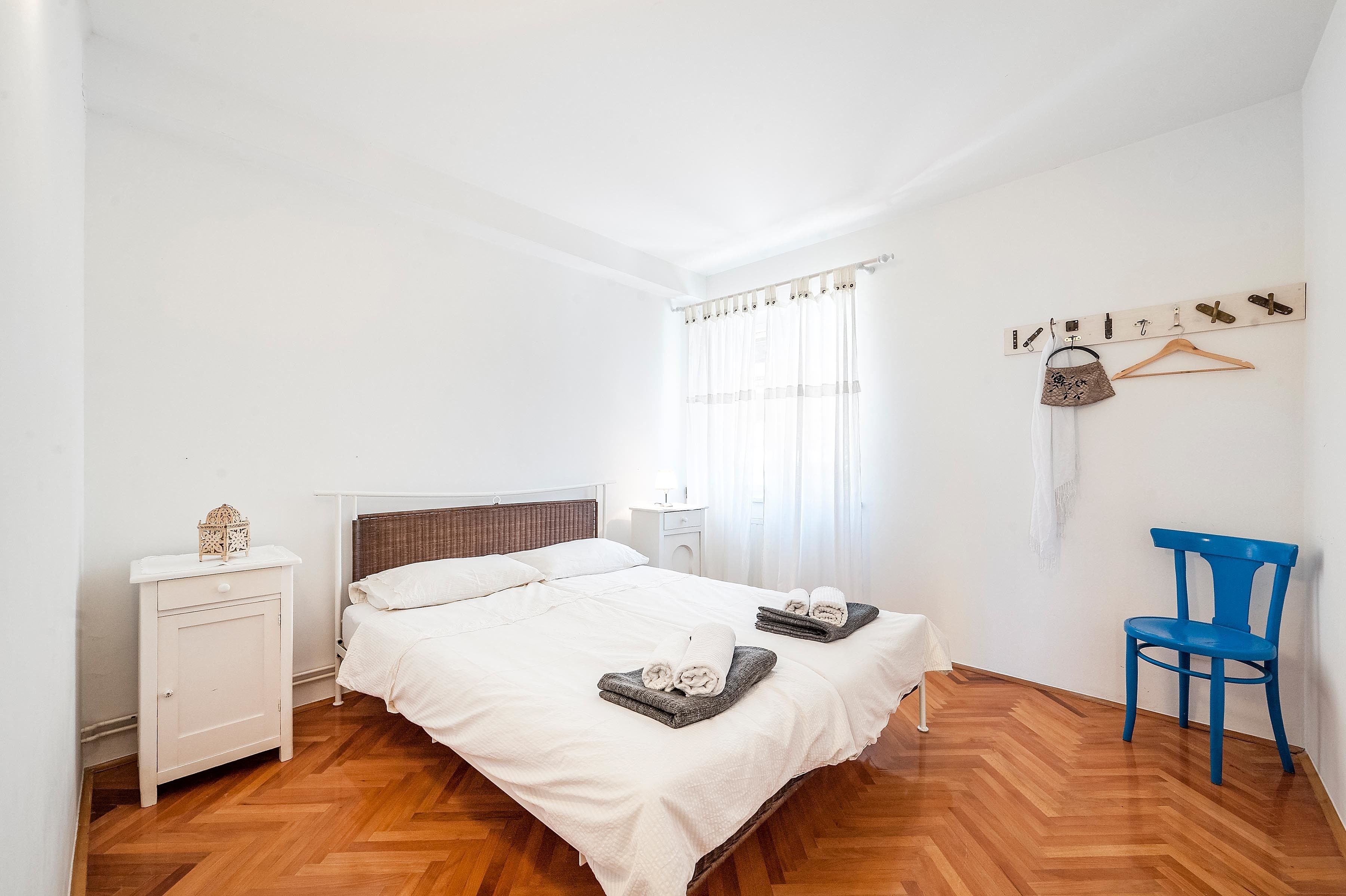 Quarto com cama, mesa de cabeceira, cadeira e cabideiro com ganchos.