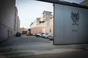 Entrada de hotel com estacionamento, portão e edifício com logotipo em brasão.