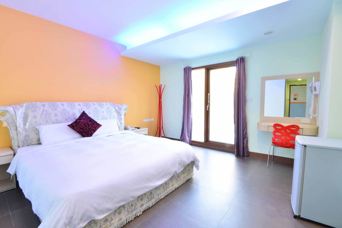 Quarto de hotel com cama, escrivaninha, cadeira e espelho de banheiro.