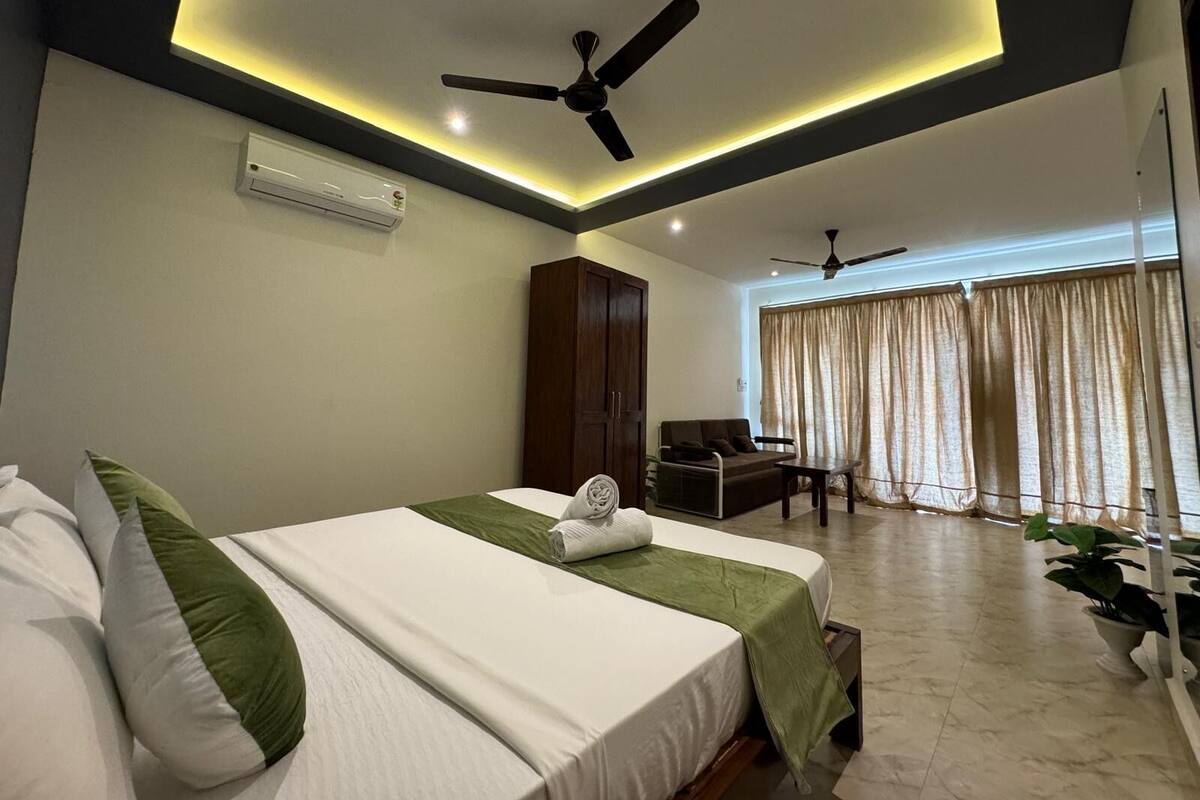 Quarto de hotel moderno com uma cama grande, um guarda-roupa, um espaço de estar e um ventilador de teto.