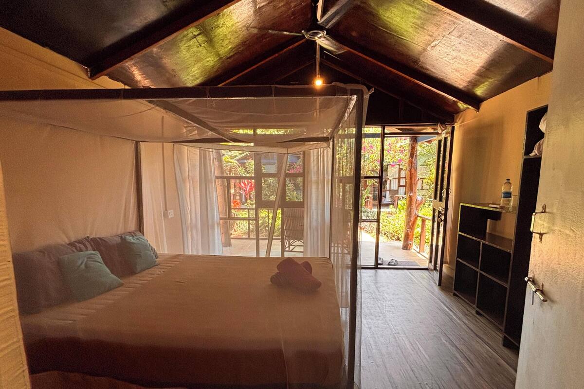 Quarto com cama de dossel, piso de madeira e vista para o jardim através de uma porta de vidro.