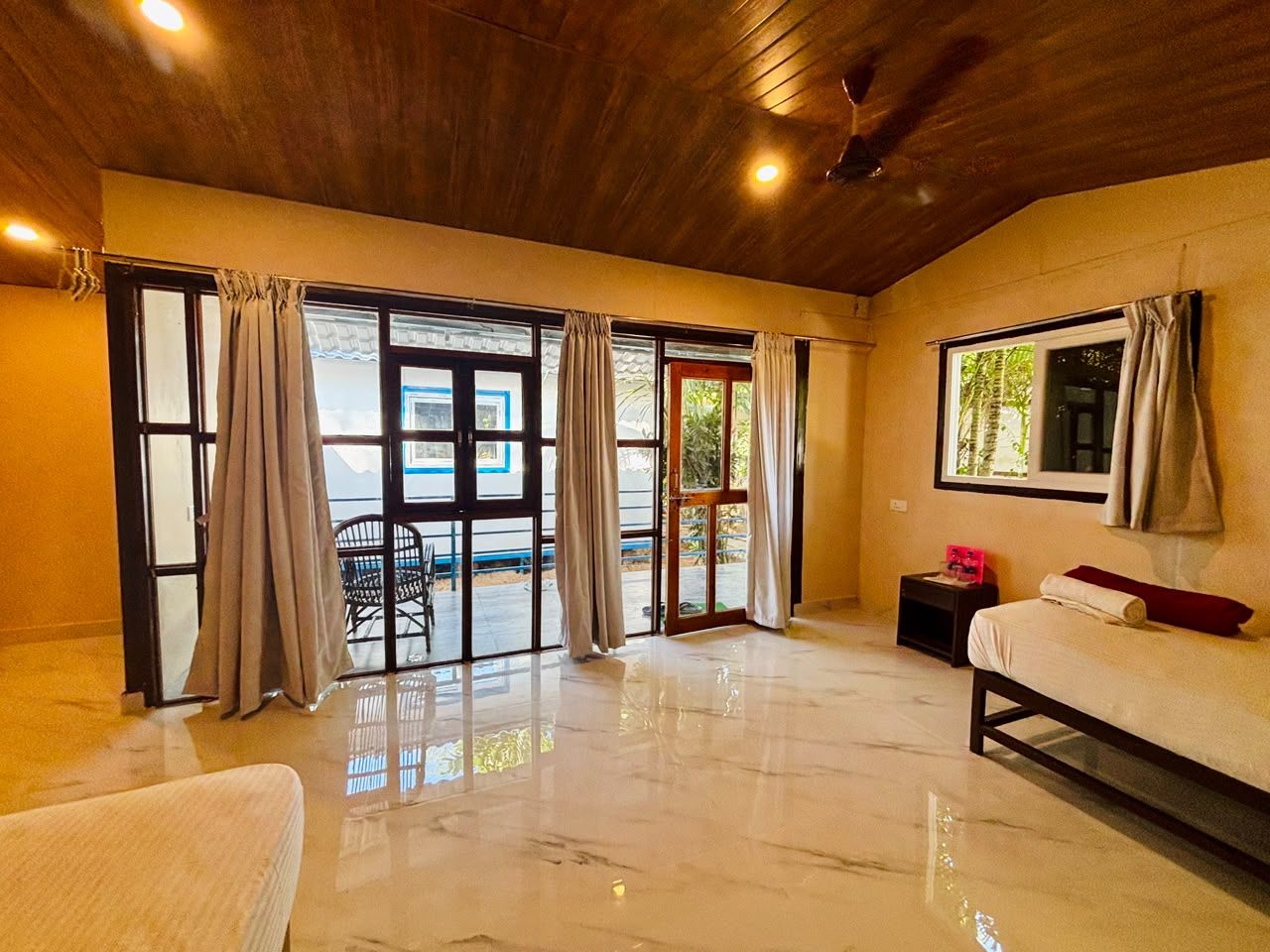 Quarto de hotel com cama, uma mesinha e vista através de grandes portas de vidro.