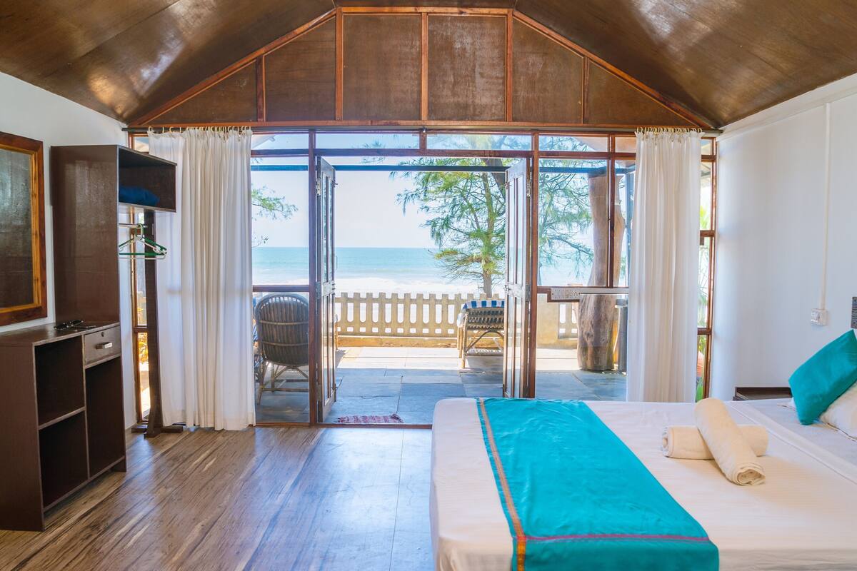 Quarto com cama, escrivaninha e vista para a praia.