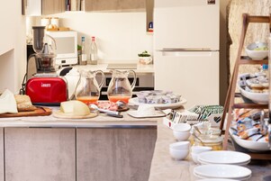 Uma bancada de cozinha com uma torradeira vermelha, um liquidificador, um jarro de suco de laranja e diversos itens de café da manhã.