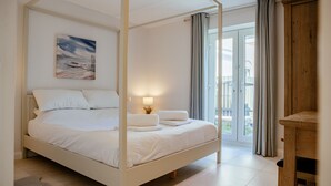 Uma cama com dossel, roupa de cama branca, um abajur e um quadro na parede.