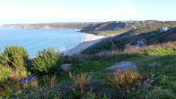 Paisagem costeira com praia, áreas gramadas e casas dispersas.