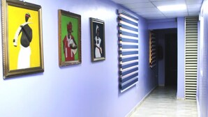 Um corredor com três obras de arte emolduradas na parede, uma janela veneziana à direita e piso de azulejos.
