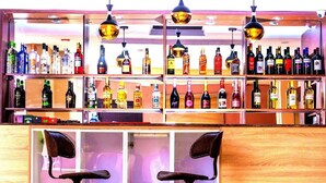 Uma área de bar com várias prateleiras cheias de garrafas de bebidas, dois bancos e luminárias pendentes.