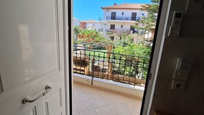 Vista de varanda com piso de azulejos, porta branca e área externa visível, com edifícios e vegetação.