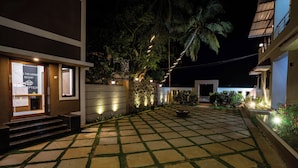 Um pátio bem iluminado com piso xadrez, uma palmeira e um edifício com área de recepção.