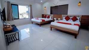 Quarto de hotel com duas camas, uma escrivaninha, ventoinha no teto, ar condicionado e janela com cortinas.