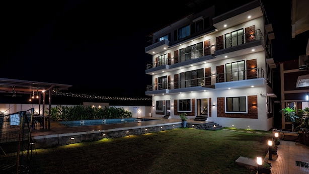 Um edifício moderno de vários andares com piscina, iluminação externa e um gramado bem cuidado.