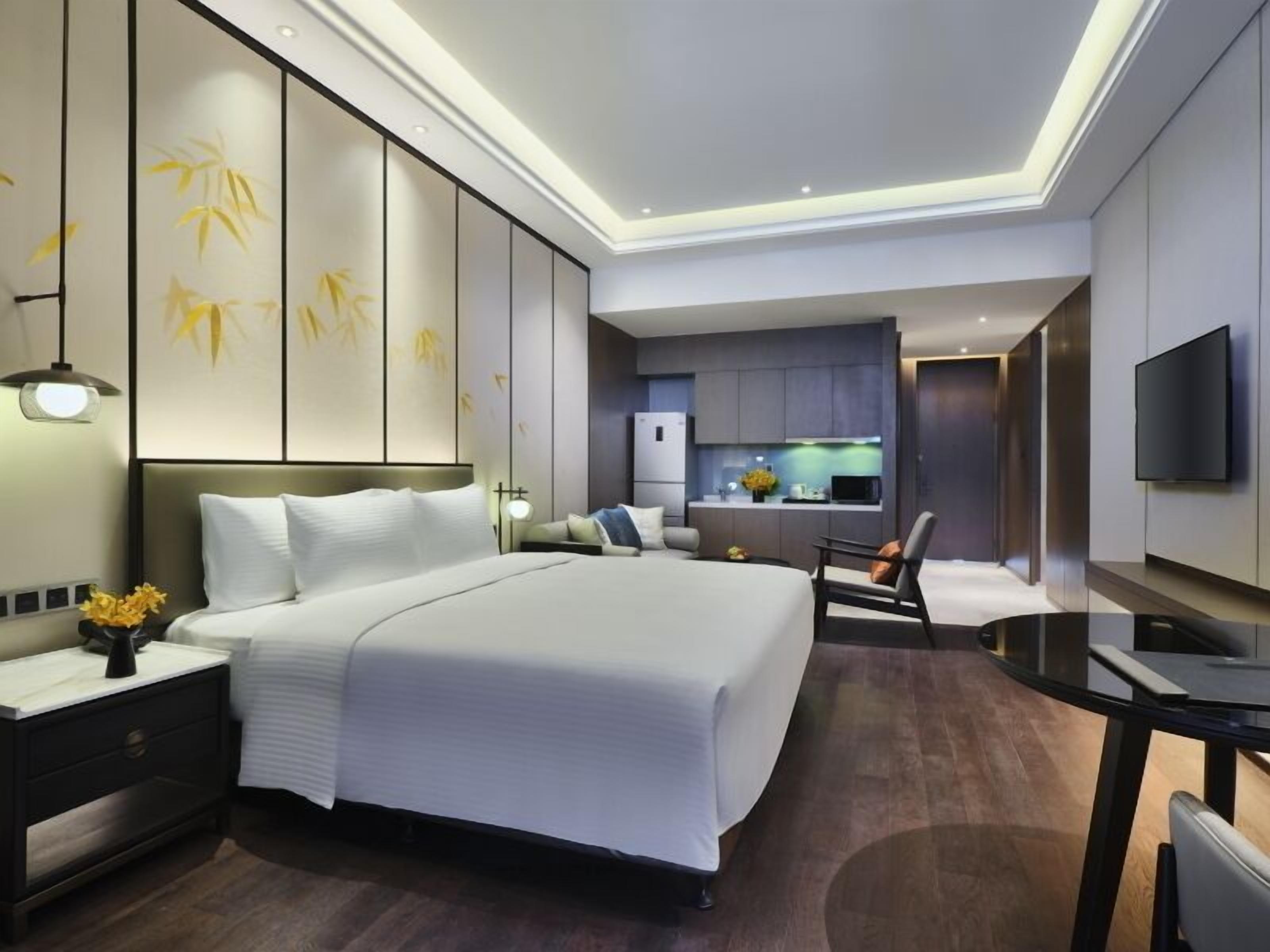 Quarto de hotel moderno com uma cama grande, uma escrivaninha, uma cadeira, uma televisão e uma kitchenette.
