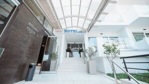 Entrada moderna de hotel com marquise de vidro, escadaria e placa indicando o restaurante 'Agimini'.