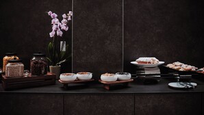 Disposição de buffet com diversos alimentos e uma orquídea em vaso.